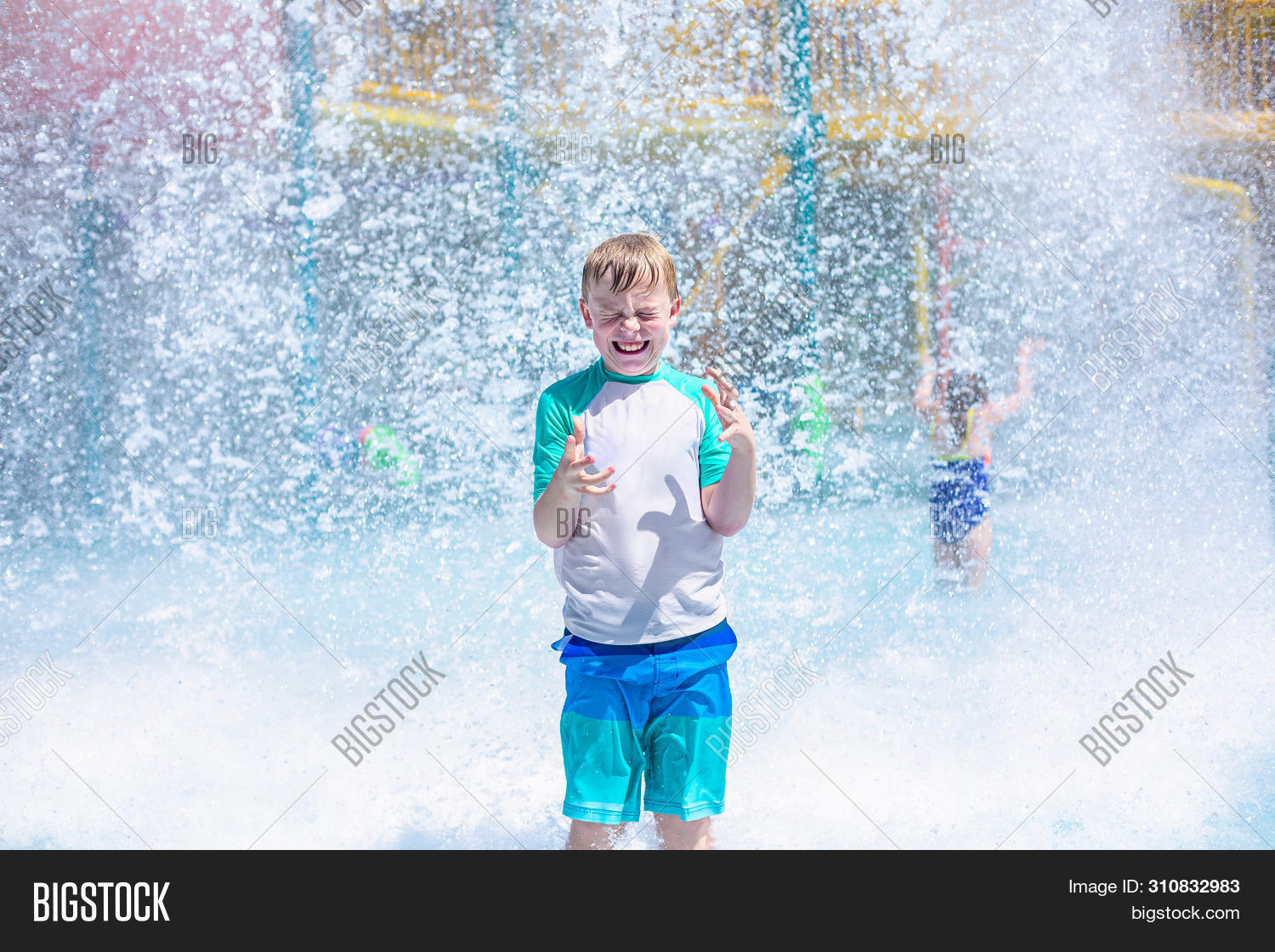 Young boy getting soaking wet while at an outdoor water park. Lots of ...
