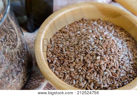 Close up of brown flax seeds in wooden bowl and flaxseed oil on a rustic table. Superfood ...