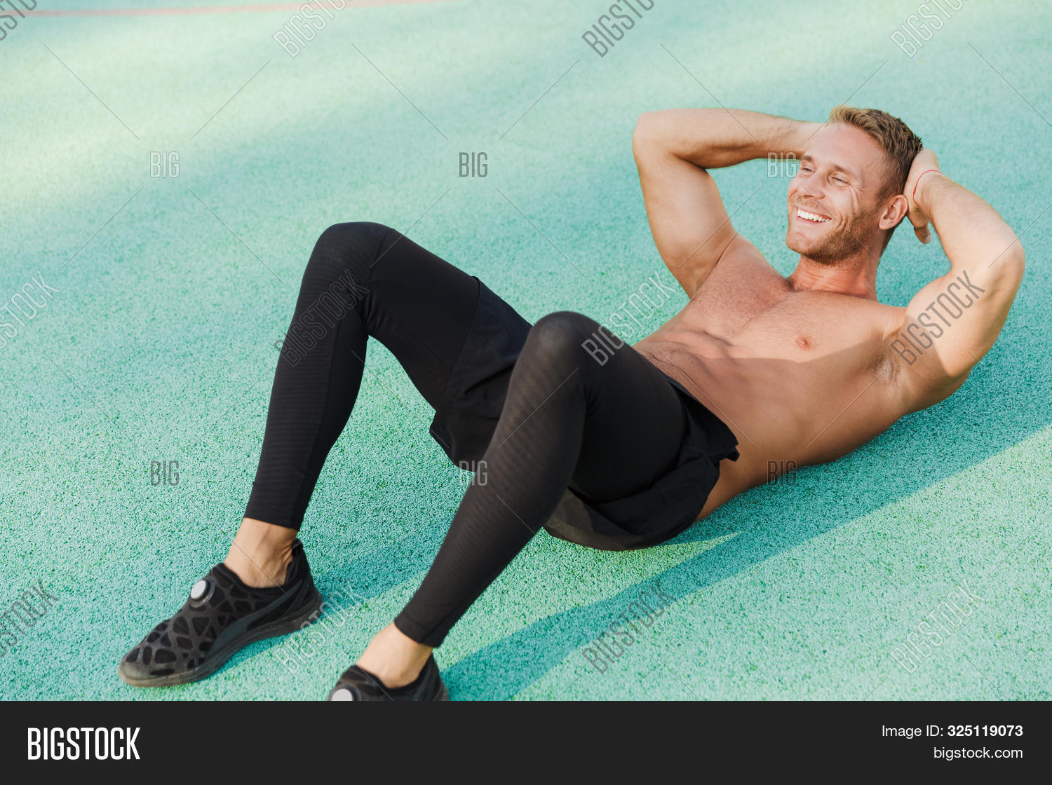 Image of caucasian shirtless man lying at green sports ground and doing ...