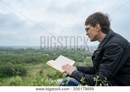 Man Reading Book In Green Hilly Field. Side View Of Young Handsome Man ...