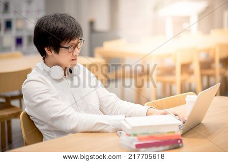 Young Asian university student working with laptop computer and book in ...