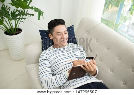 Handsome young man at home writing writing down thoughts in journal on ...