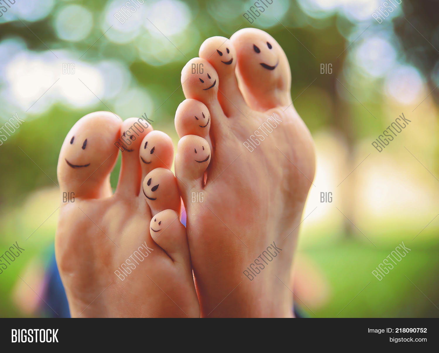 smiley faces on a pair of feet on all ten toes in a park on a hot ...